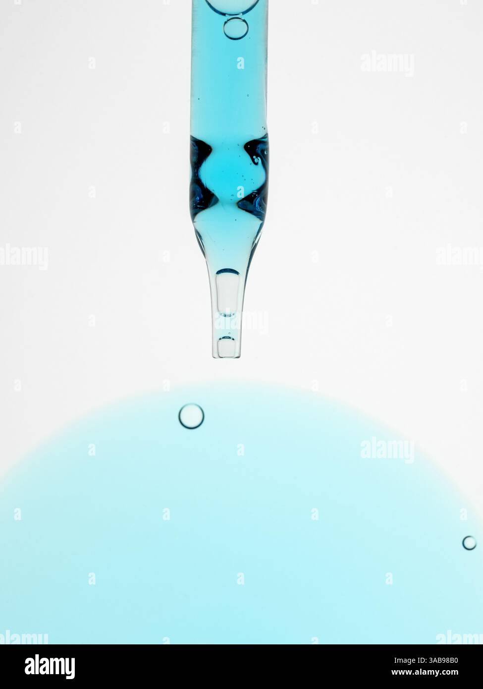 A clear pipette releases blue liquid into a pool below, creating ...