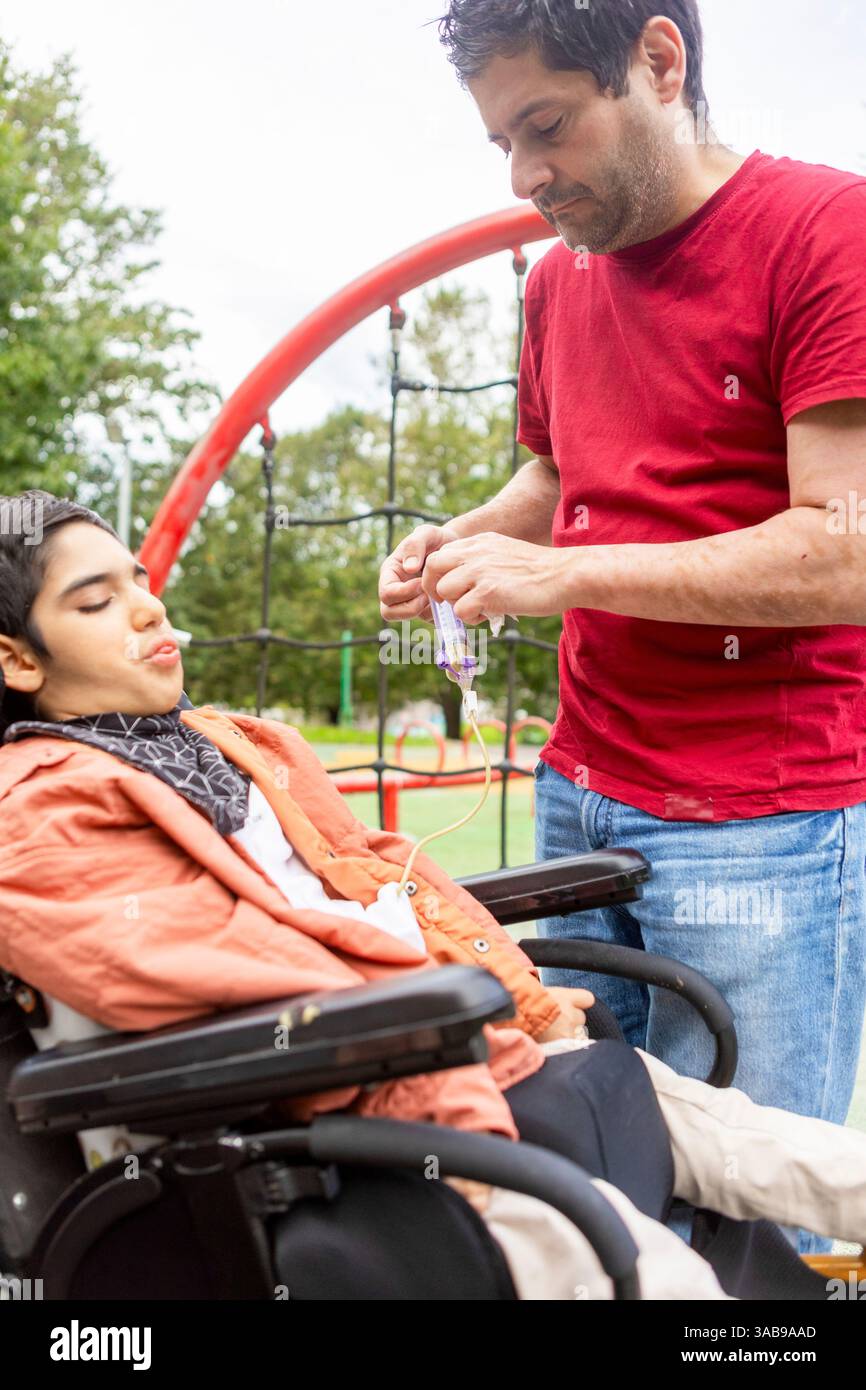 A father assists a her child with cerebral palsy in a wheelchair, using ...