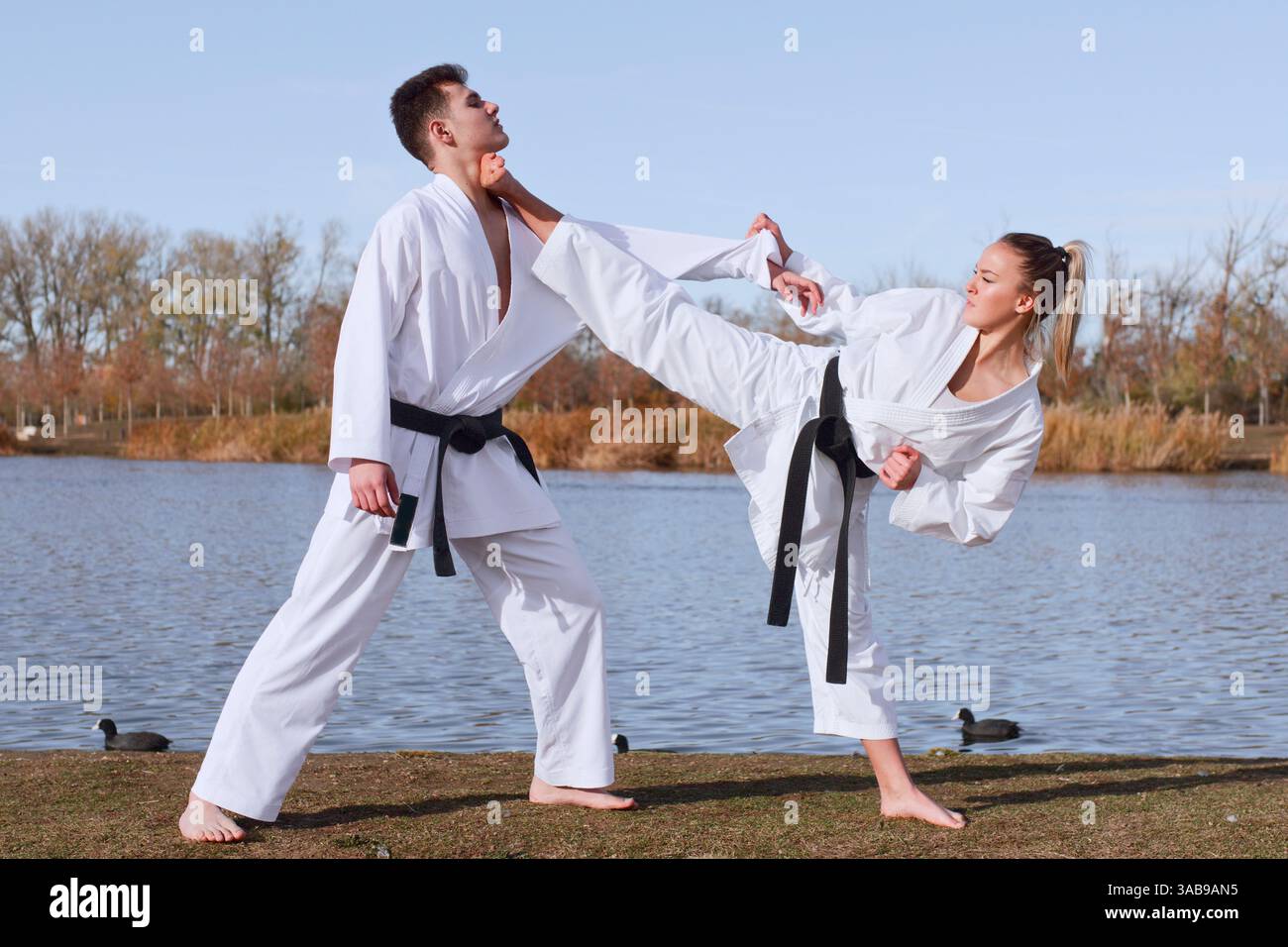 Two karate experts practice martial arts on a lakeside, wearing ...