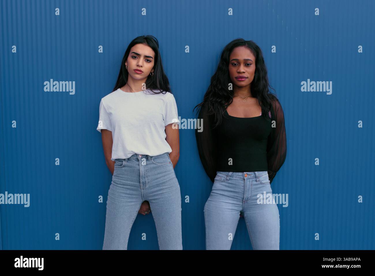 Two women pose confidently in jeans, one in a white tee and the other ...