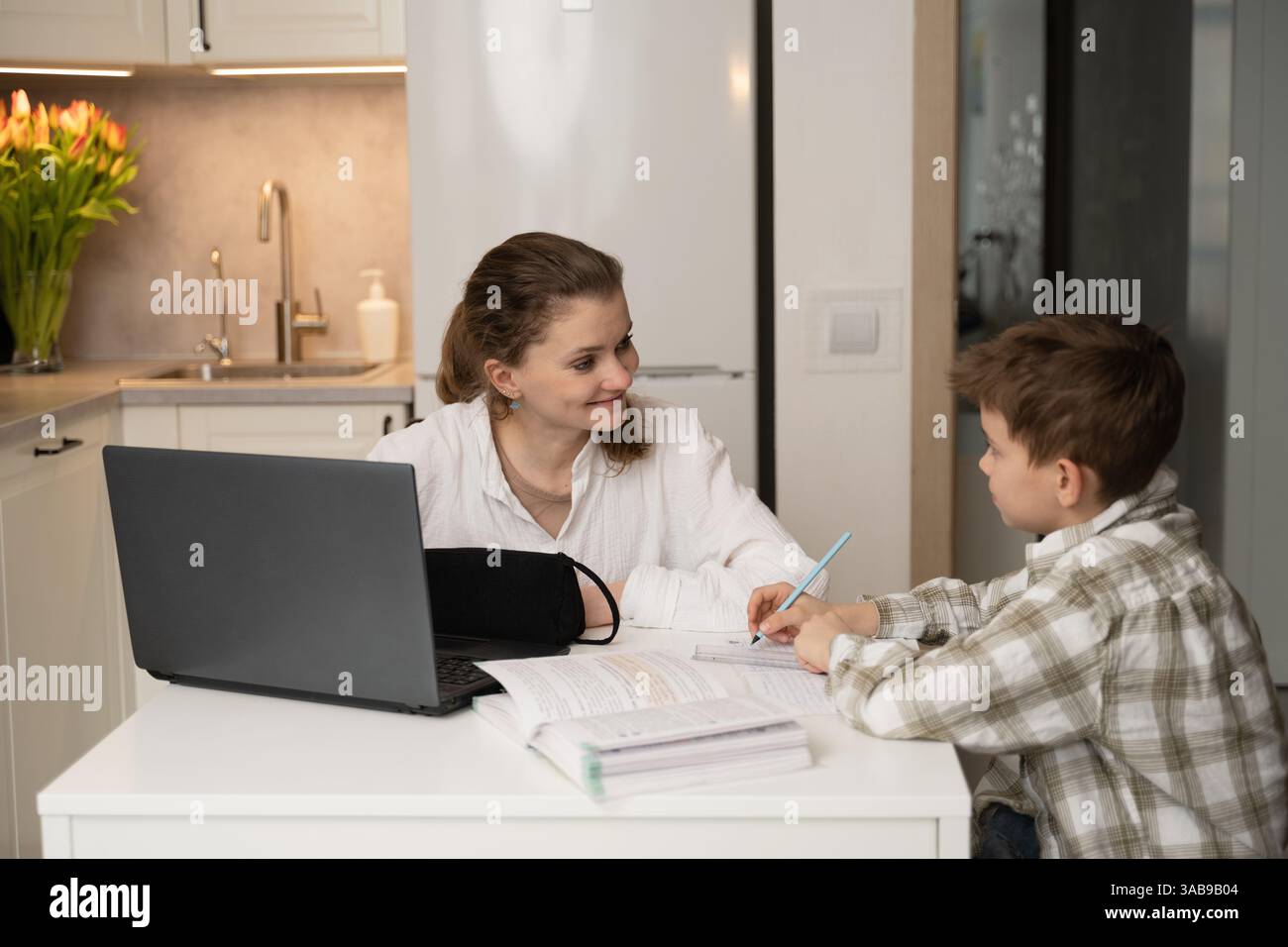 A mother guides her son in a home learning setup, featuring a laptop ...