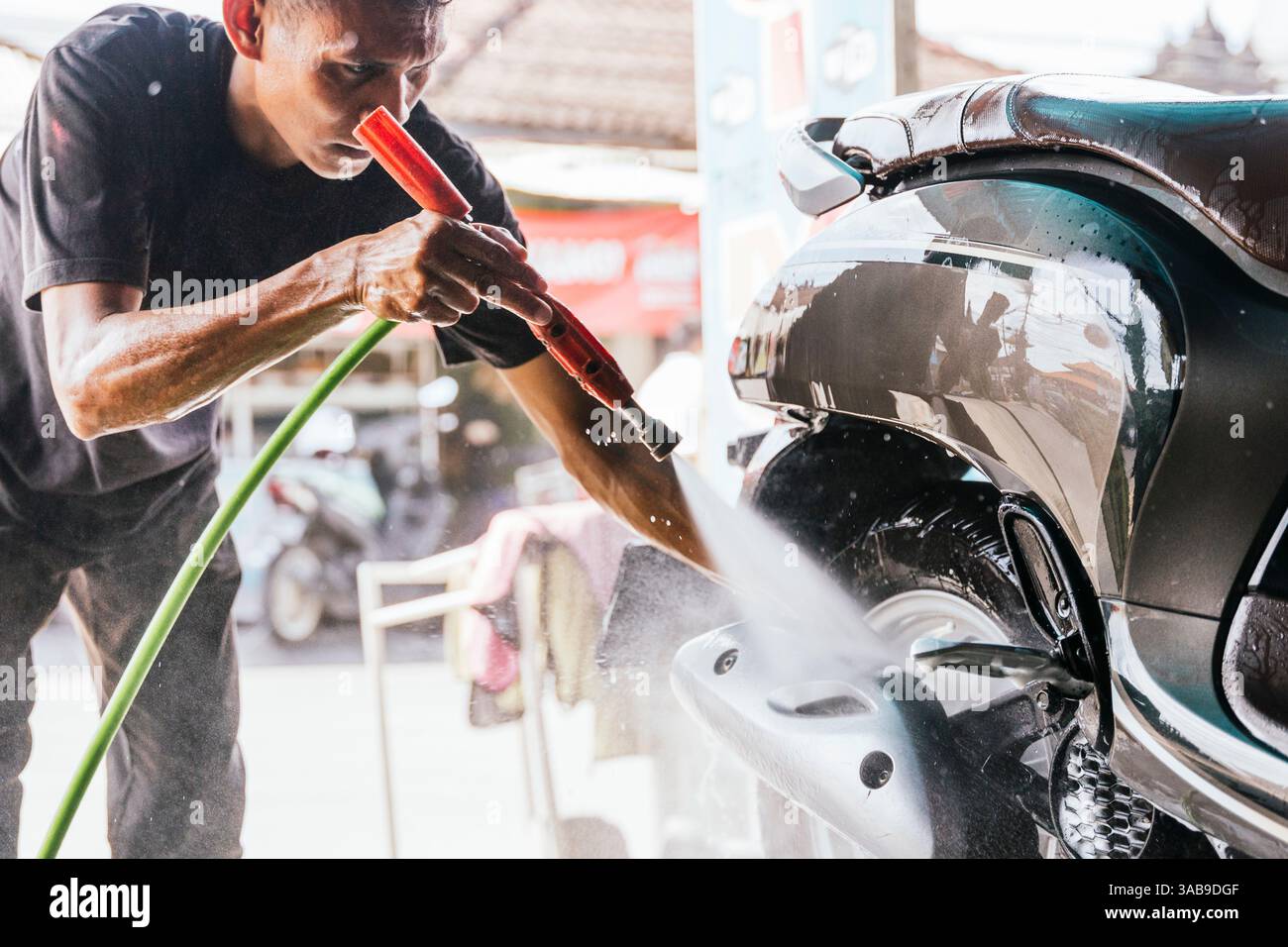 A man is meticulously cleaning a motorcycle with a water hose ...