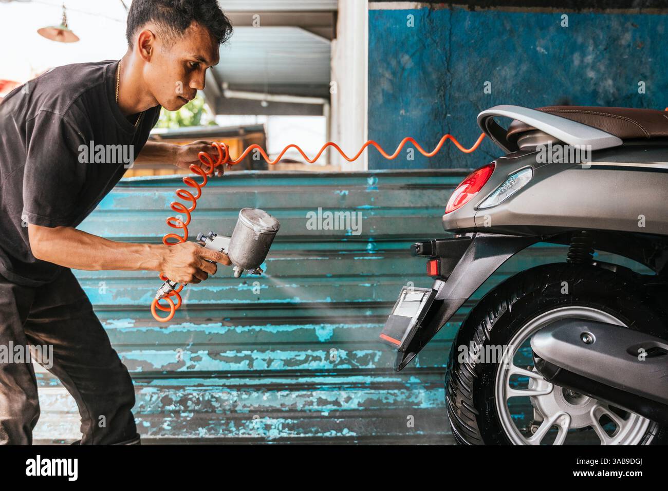 A motorcycle cleaner uses a spray gun to carefully wash a scooter ...