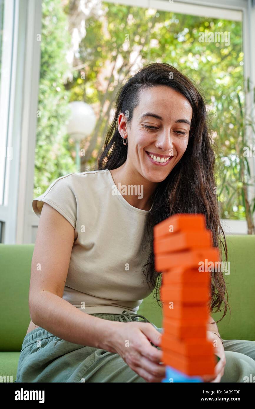 A young woman smiles while carefully playing a stacking block game ...