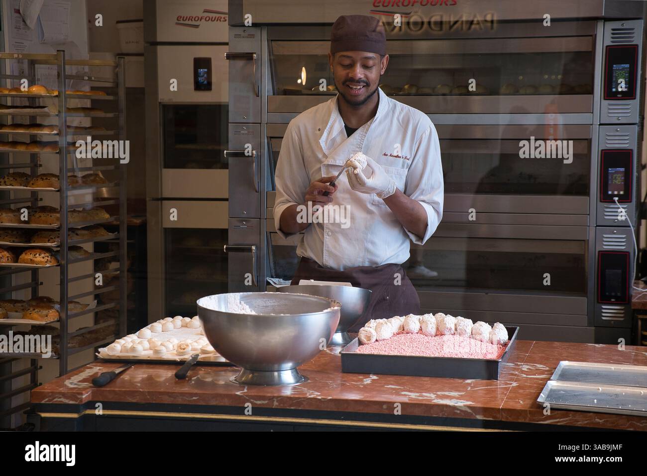 A patissier (pastry chef) making small cakes in shop kitchen in Paris ...