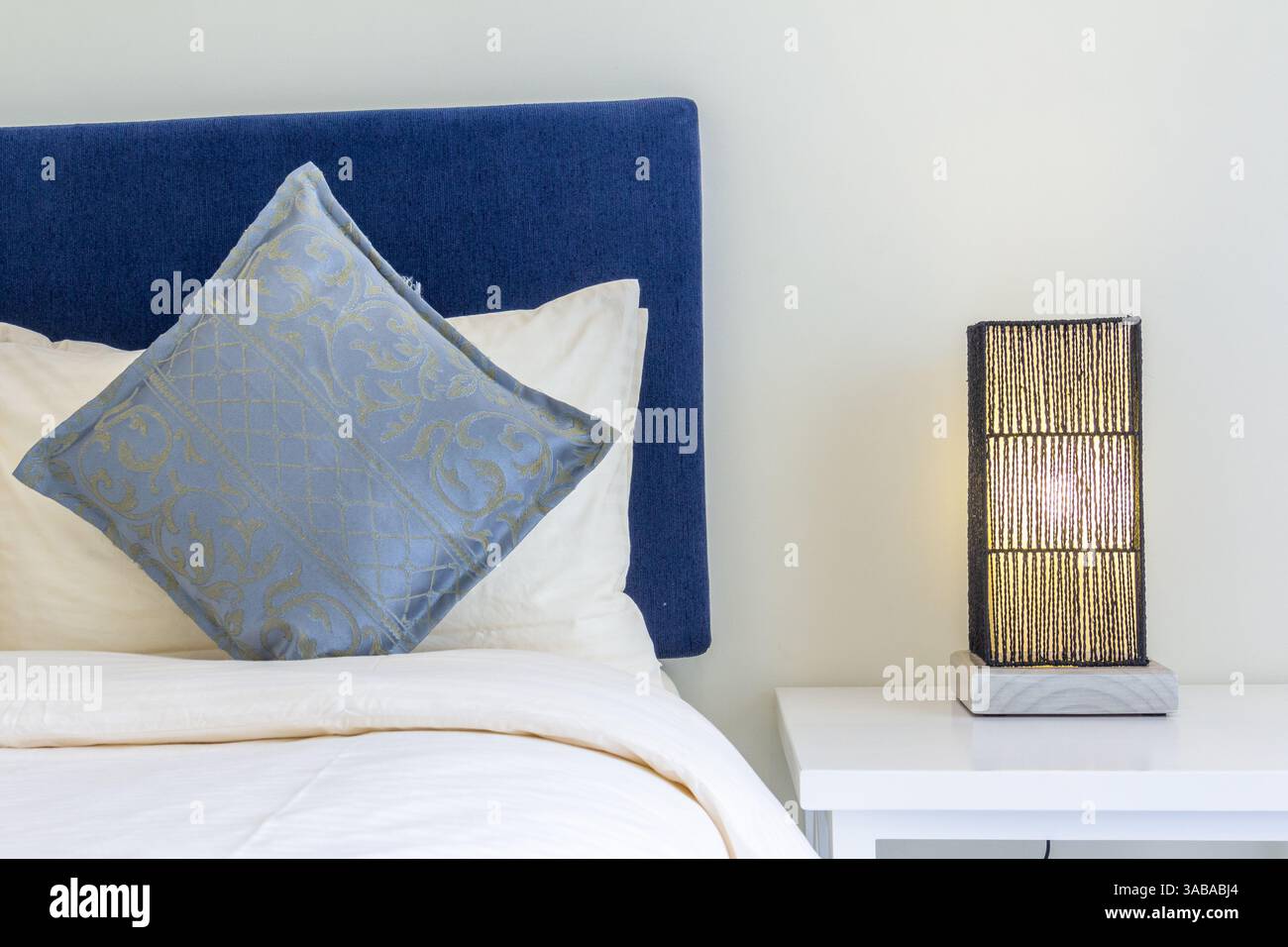 Comfy queen bed with plush pillows and blue headboard beside a modern ...
