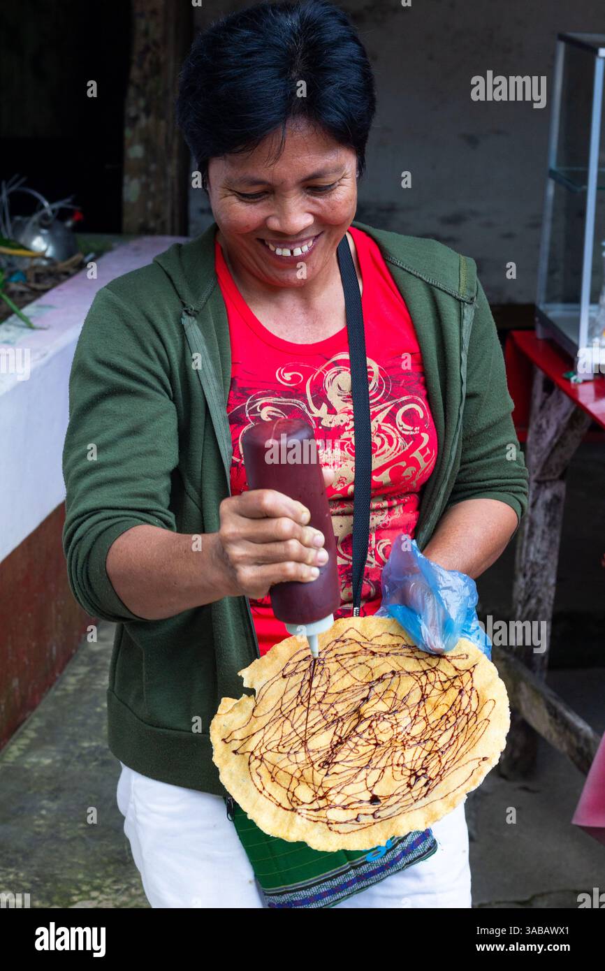 A Filipina vendor smiles while swirling sugar syrup on a kabkab, a ...
