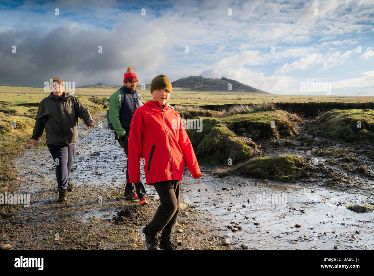 An adult and two young boys walking down a waterlogged worn eroded ...