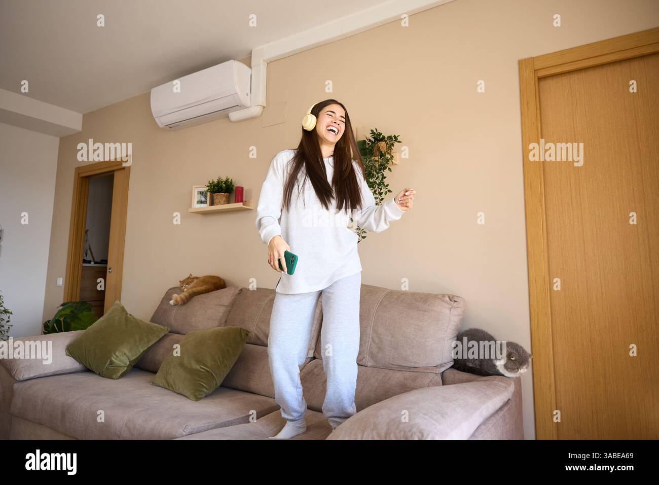 Young woman dancing on sofa listening music with headphones and ...