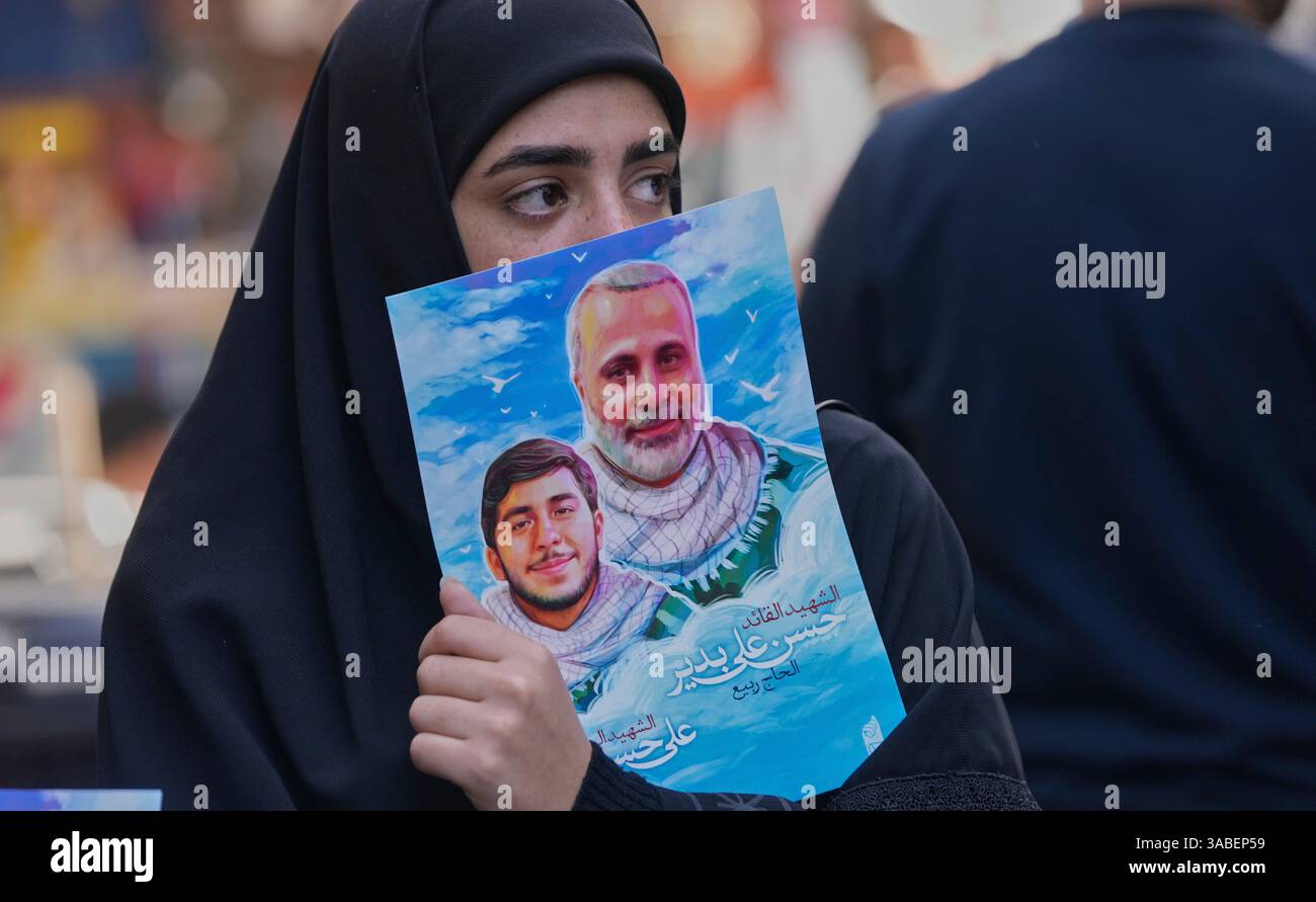 A mourner holds images of Hezbollah official Hassan Bdeir and his son ...