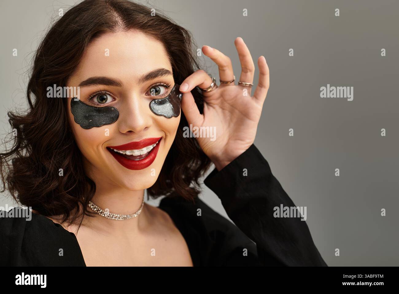 A young woman smiles playfully, showcasing her braces and bold red lips ...