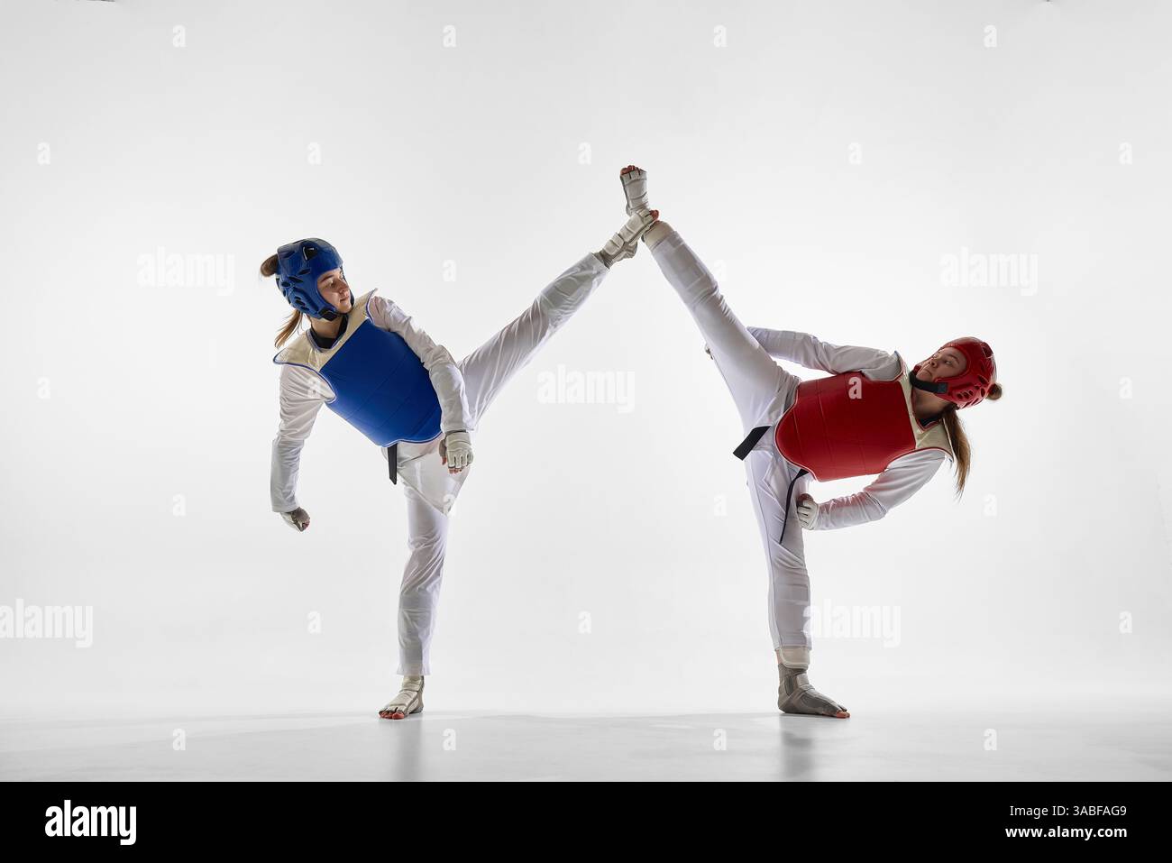 Two young women in blue and red taekwondo gear locked in mirrored kicks ...