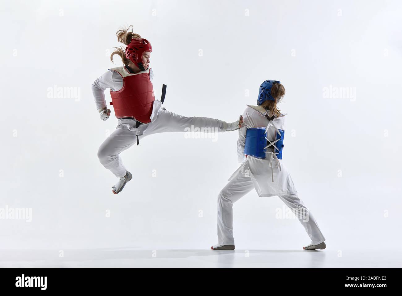 Two female taekwondo fighters crossing high kicks in mirrored motion ...