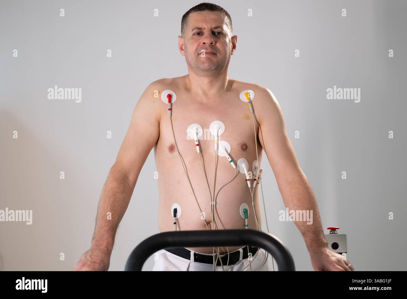 A middle-aged man is undergoing a medical stress test on a treadmill ...