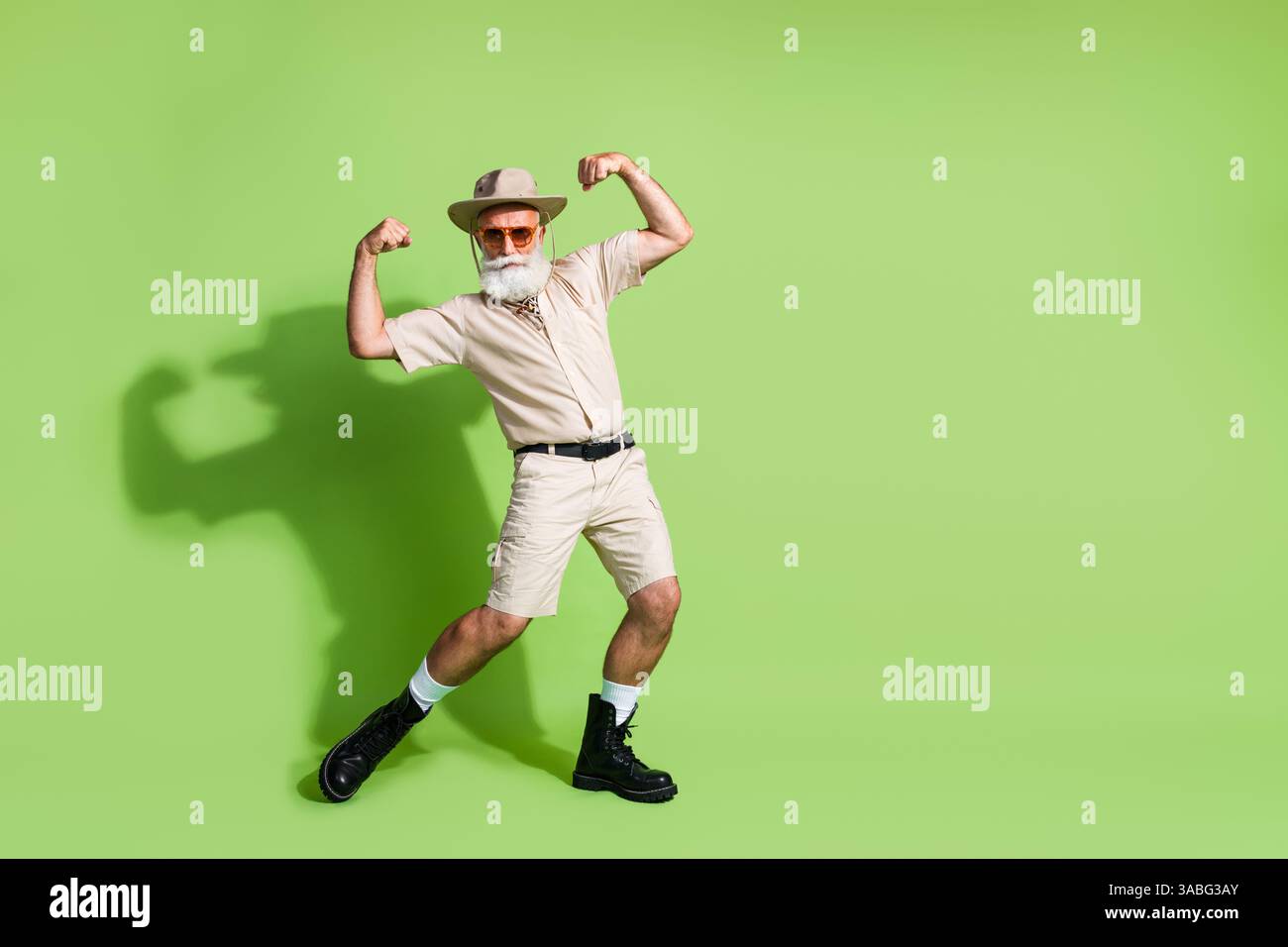Elderly explorer in stylish safari outfit poses against vibrant green ...