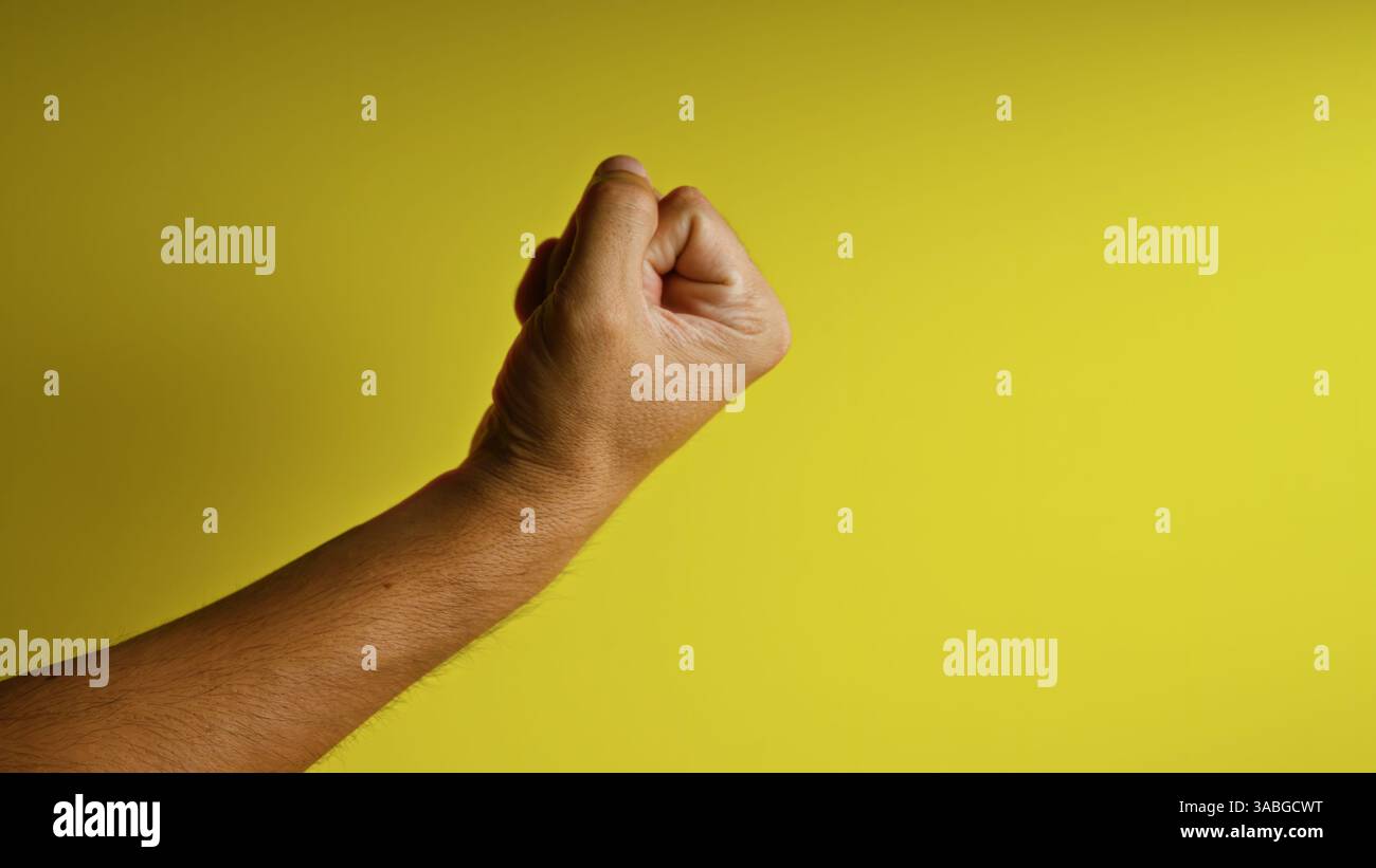 Man making a fist with his hand against a bright yellow background ...