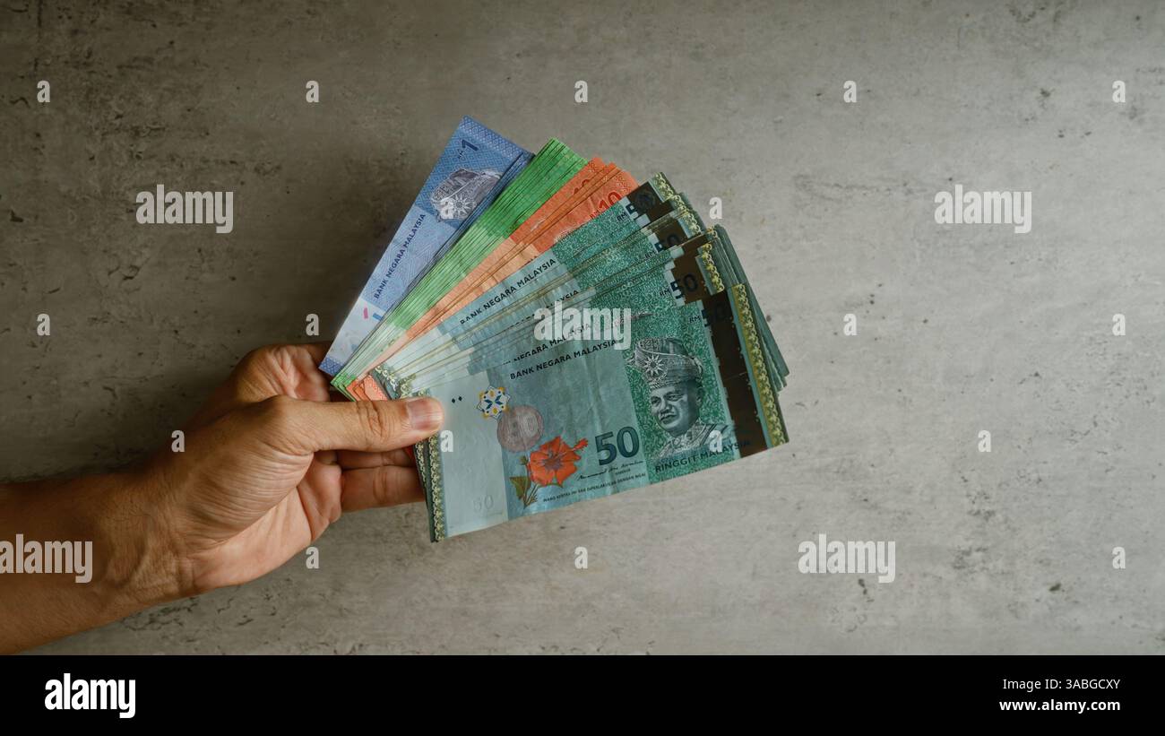 Hand holding malaysian ringgit banknotes against a concrete background ...