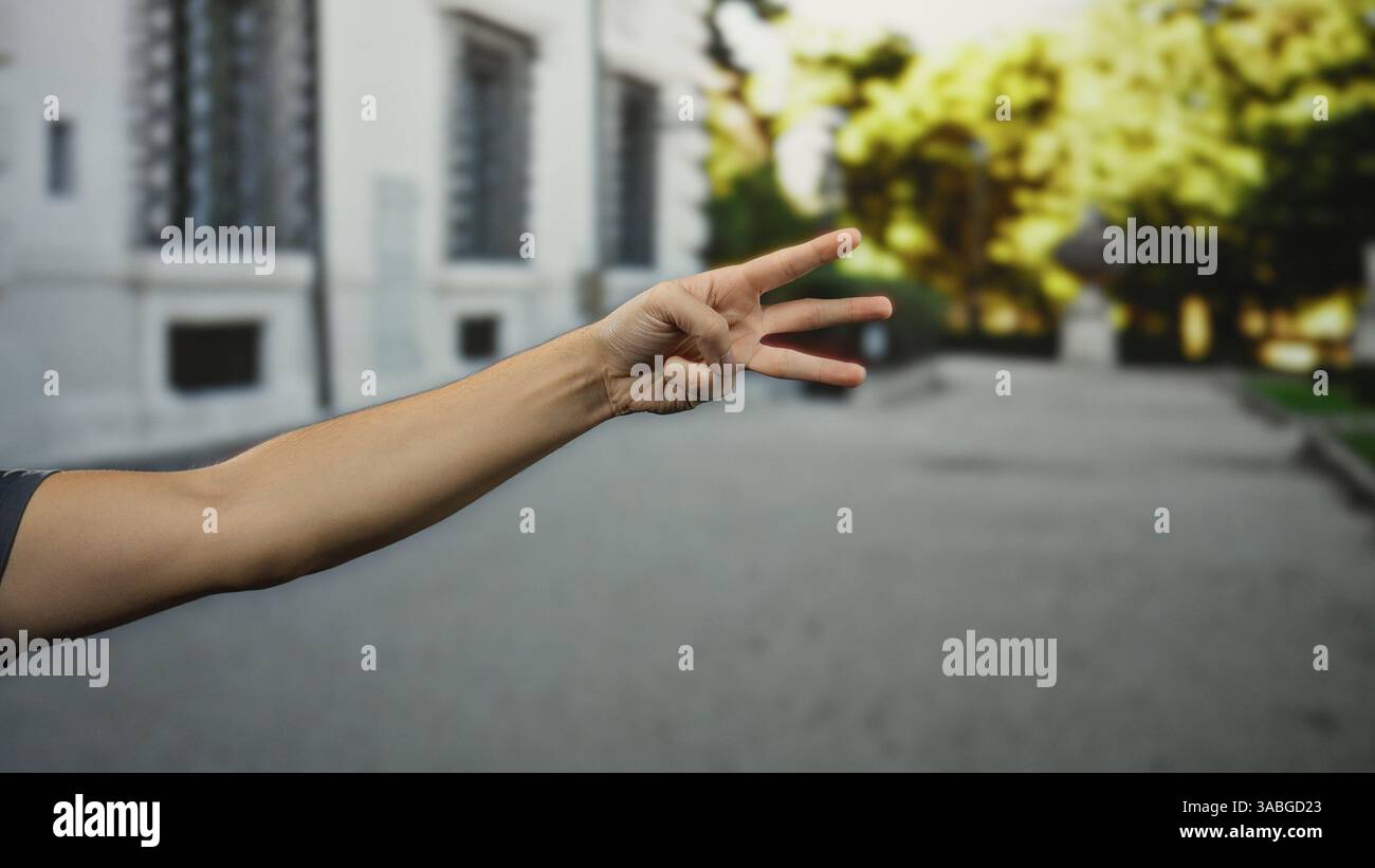 Man's hand showing three fingers in an outdoor city street on a sunny ...