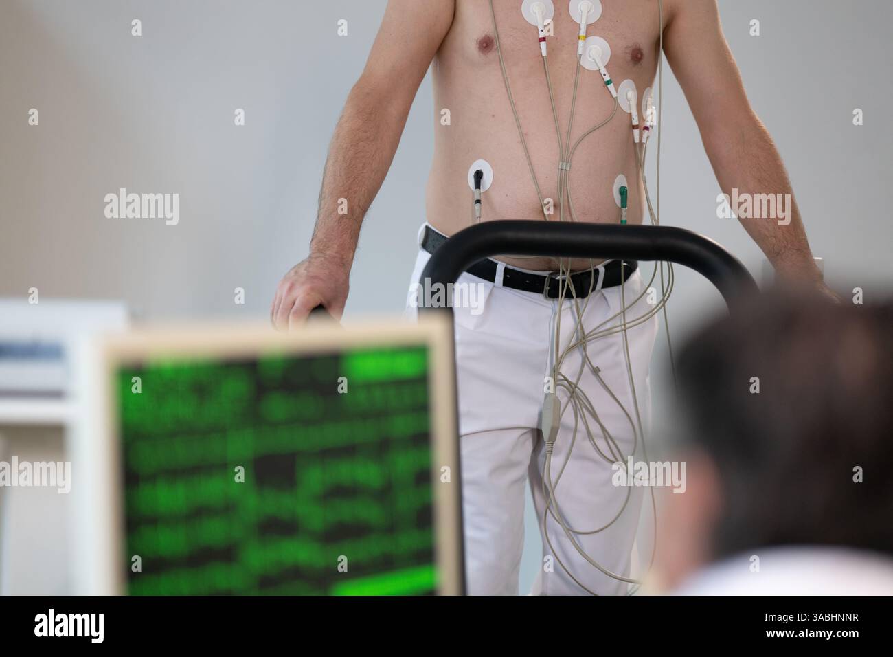 A middle-aged man is undergoing a medical stress test on a treadmill ...