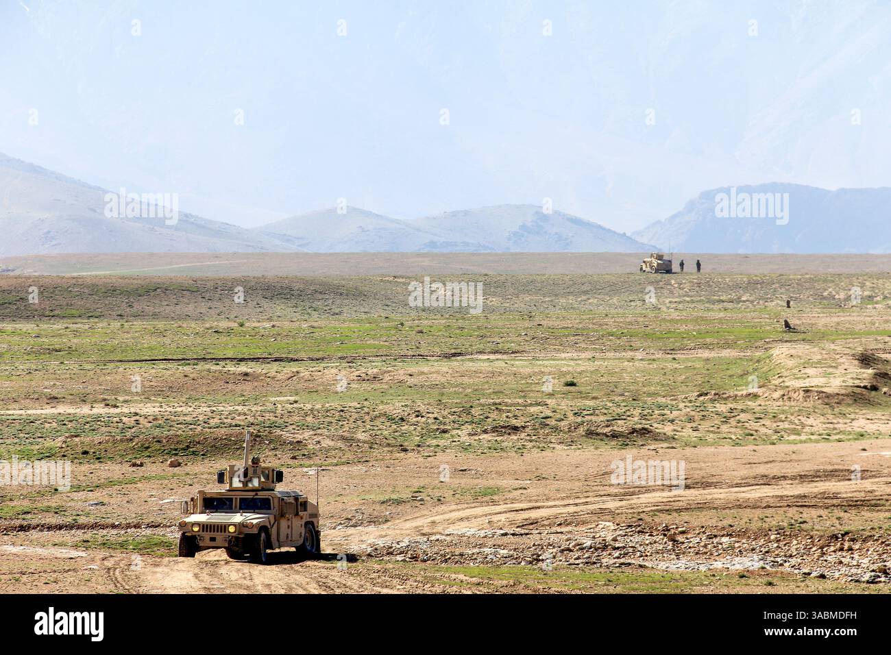 A wide view of military vehicles traversing an expansive desert terrain ...
