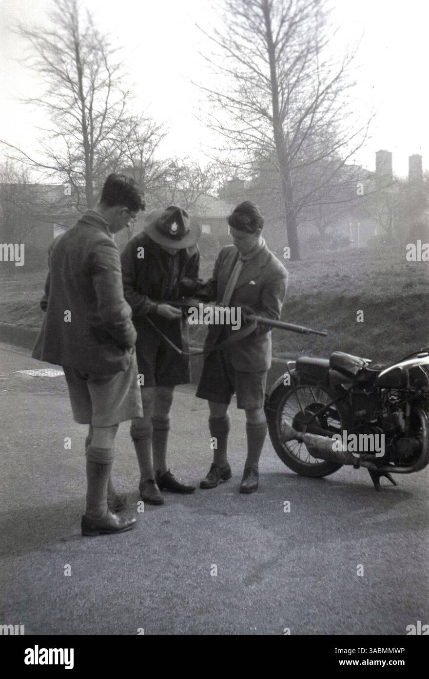 1940, historical, Britain, three scouts outside examing a rifle, beside a motorcycle of the era ...