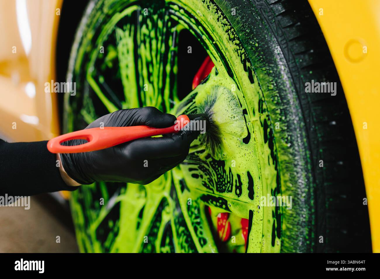 Spraying green detergent on tire of a yellow sports car using a spray ...