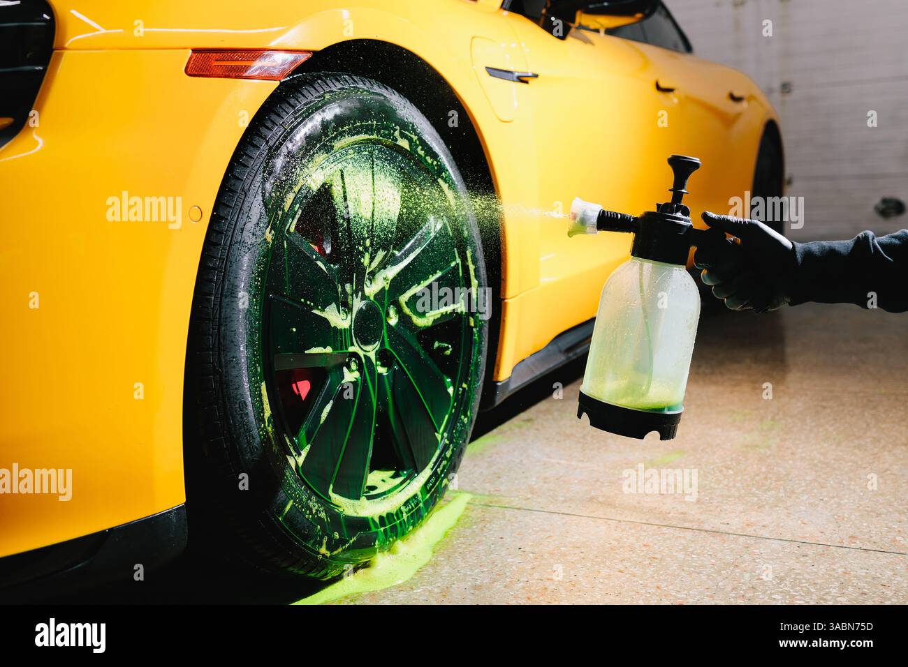 Worker cleans the tire of a yellow car using a spray with soap solution ...