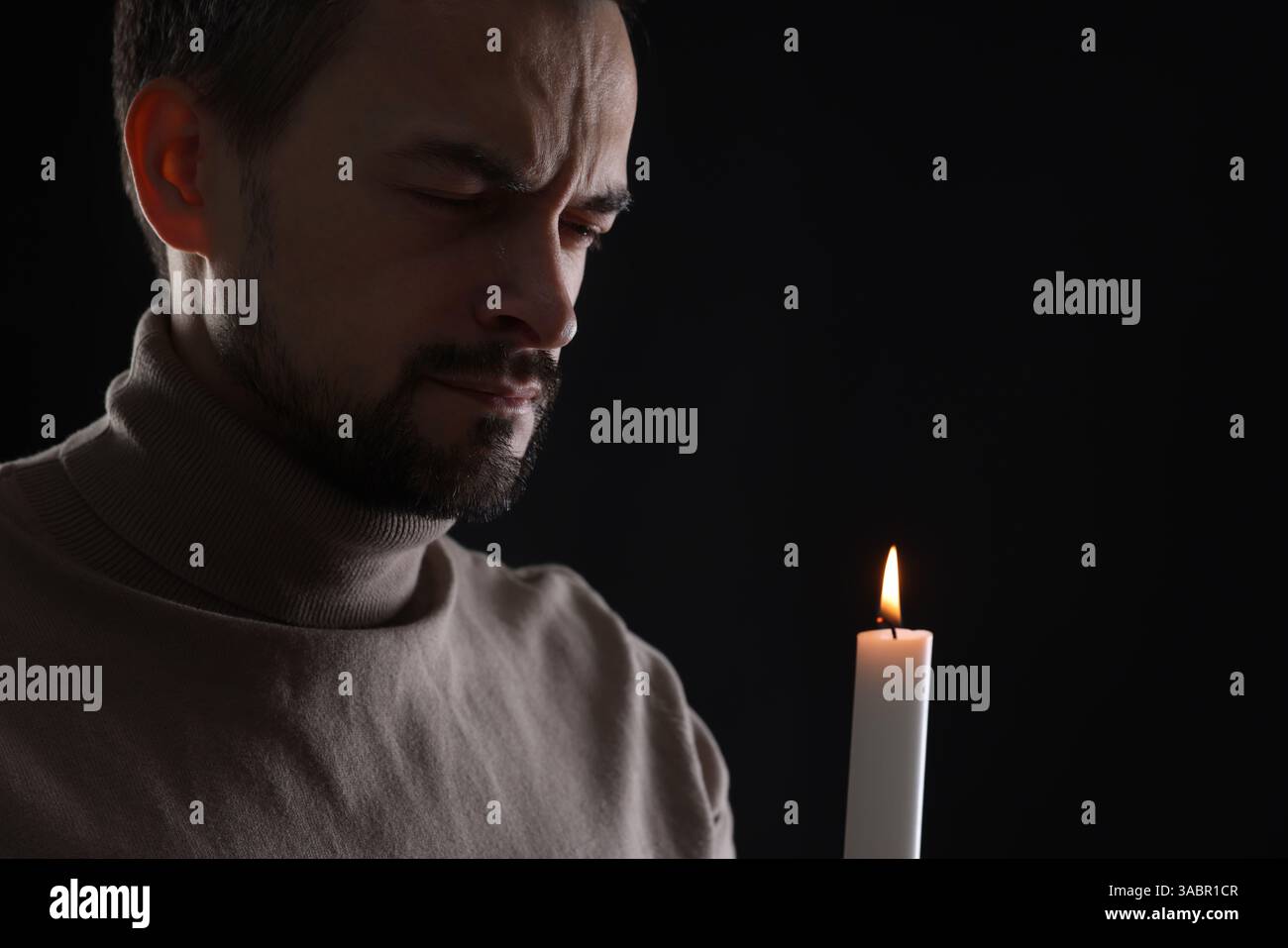 Sad man with burning candle crying on black background, space for text ...