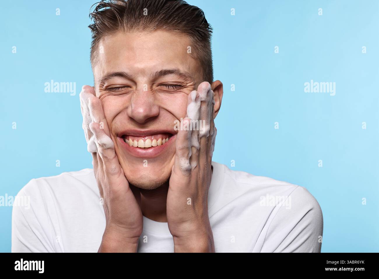 Smiling man washing his face with cleansing foam on light blue background Stock Photo - Alamy
