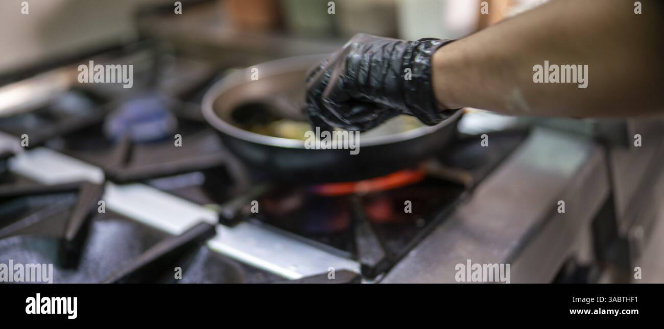 Professional chef wearing black gloves cooking indian food in a pan on ...