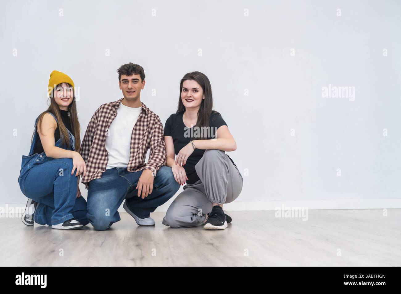 Three young dancers are crouching and posing in a dance studio, ready ...