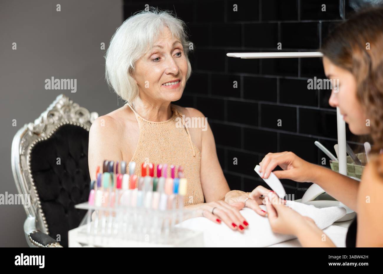 Female manicurist shaping and polishing nails to smiling elderly woman ...