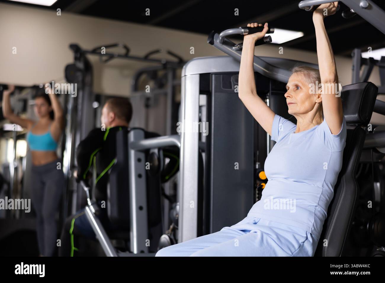 Focused mature female athlete using overhead press machine in gym Stock ...