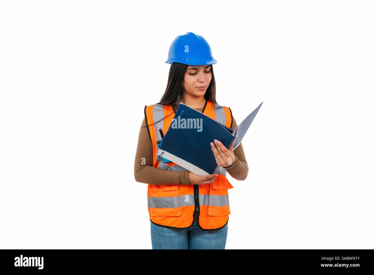 Young Latin construction engineer reading a blueprint while wearing an orange safety vest and a ...