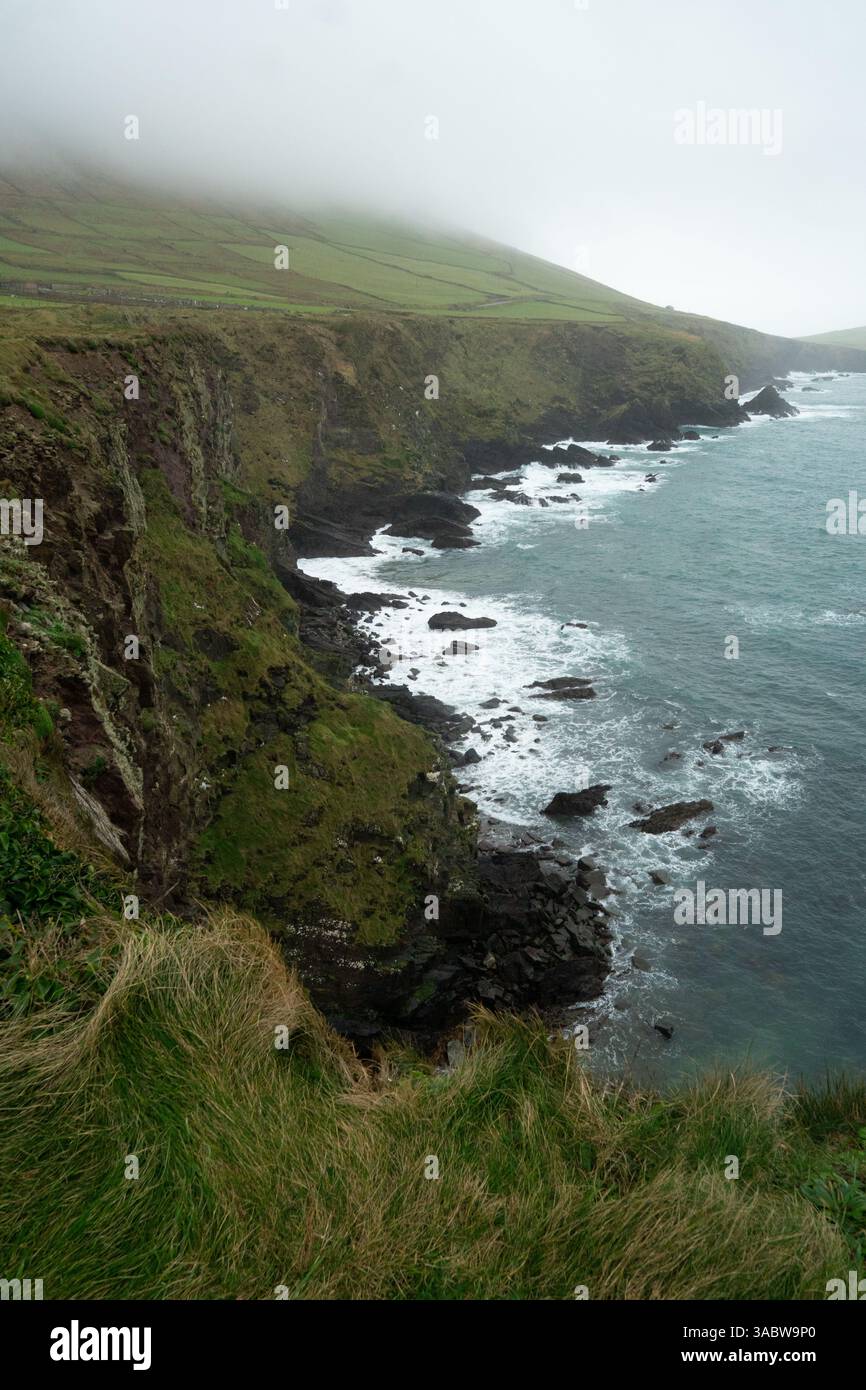 Irish cliffside with green meadows on the left and ocean waves on the ...