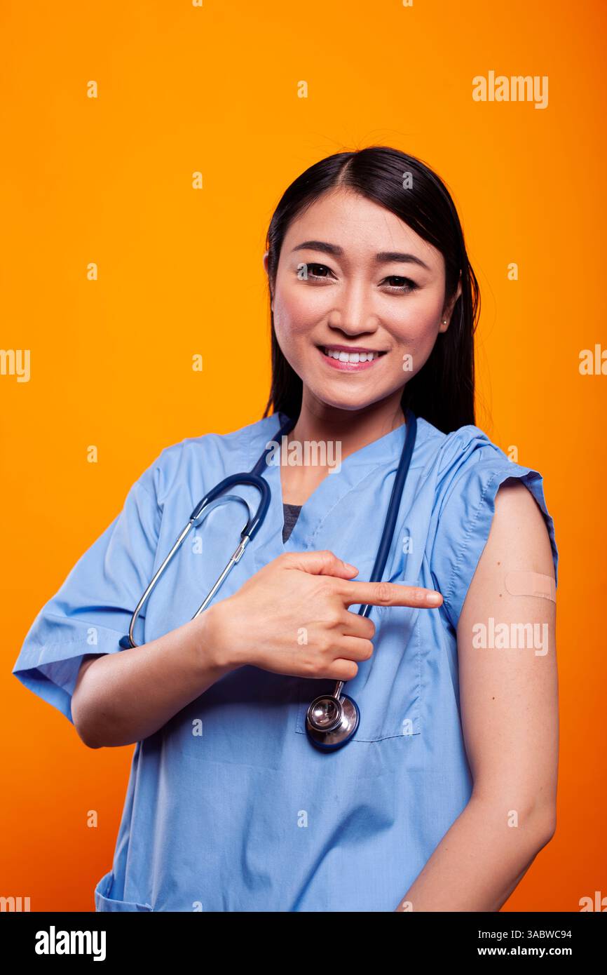 Asian female nurse in medical uniform, displaying her vaccinated arm ...