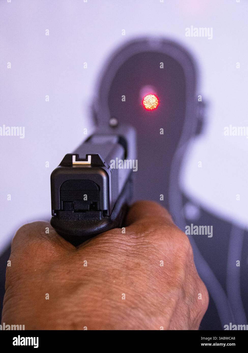 A man aims a black handgun with a laser sight at the head on a paper ...
