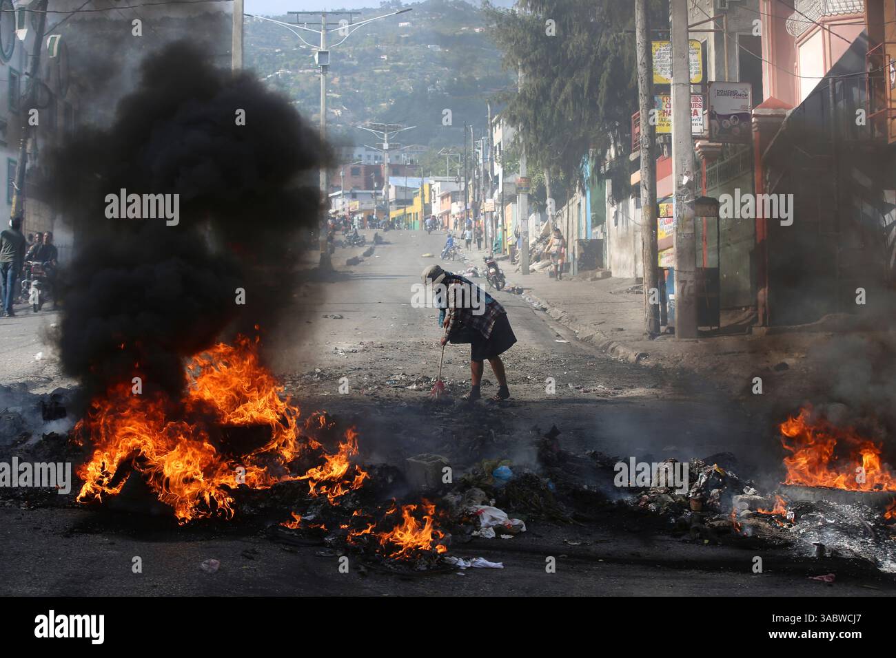 A woman sweeps debris next to a blazing barricade set up by ...