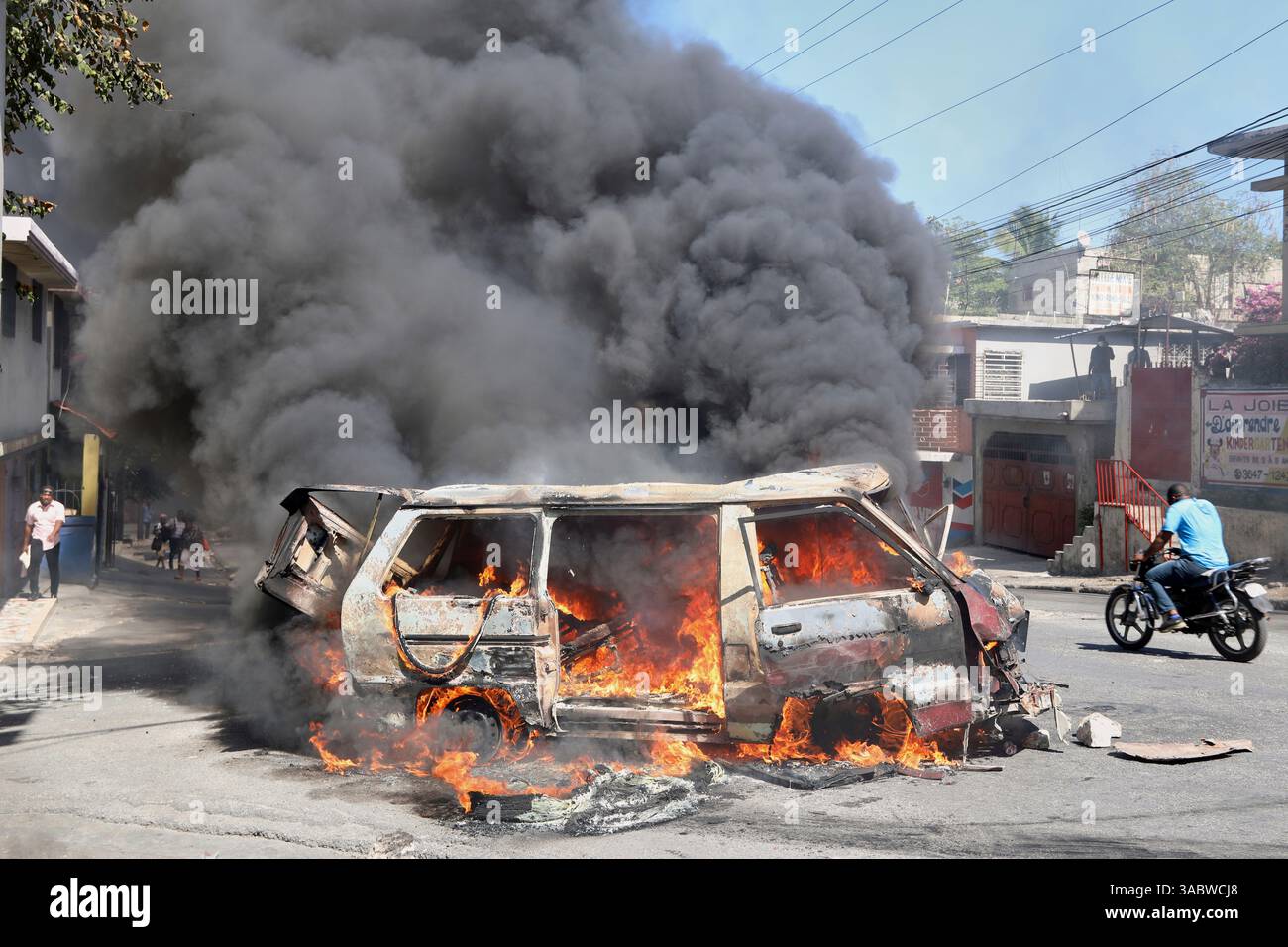 A motorcyclist rides past a burning car during a protest against ...