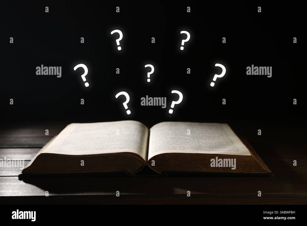 Question marks over open book on wooden table against black background ...