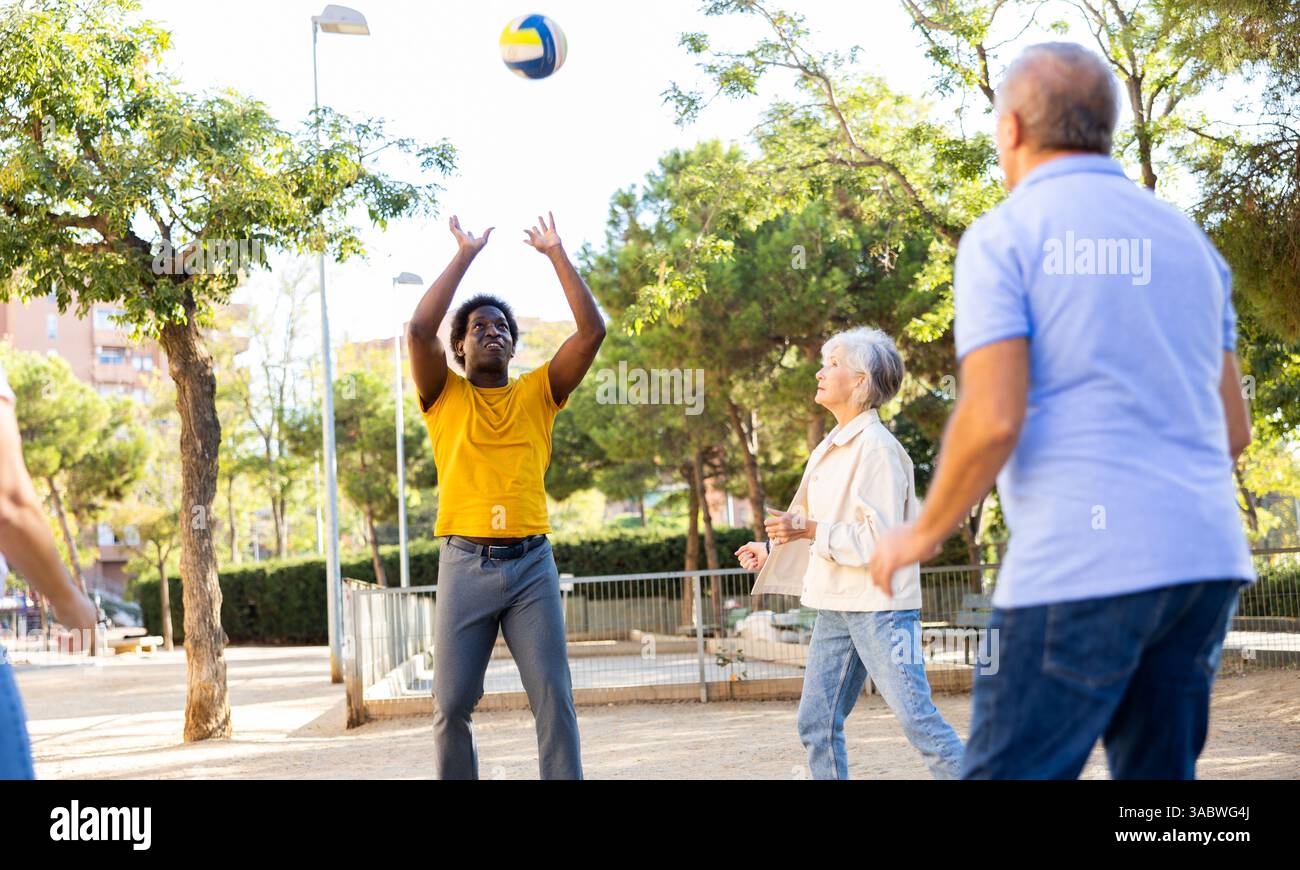 Joyful multiracial group of mature adult people playing volleyball game ...