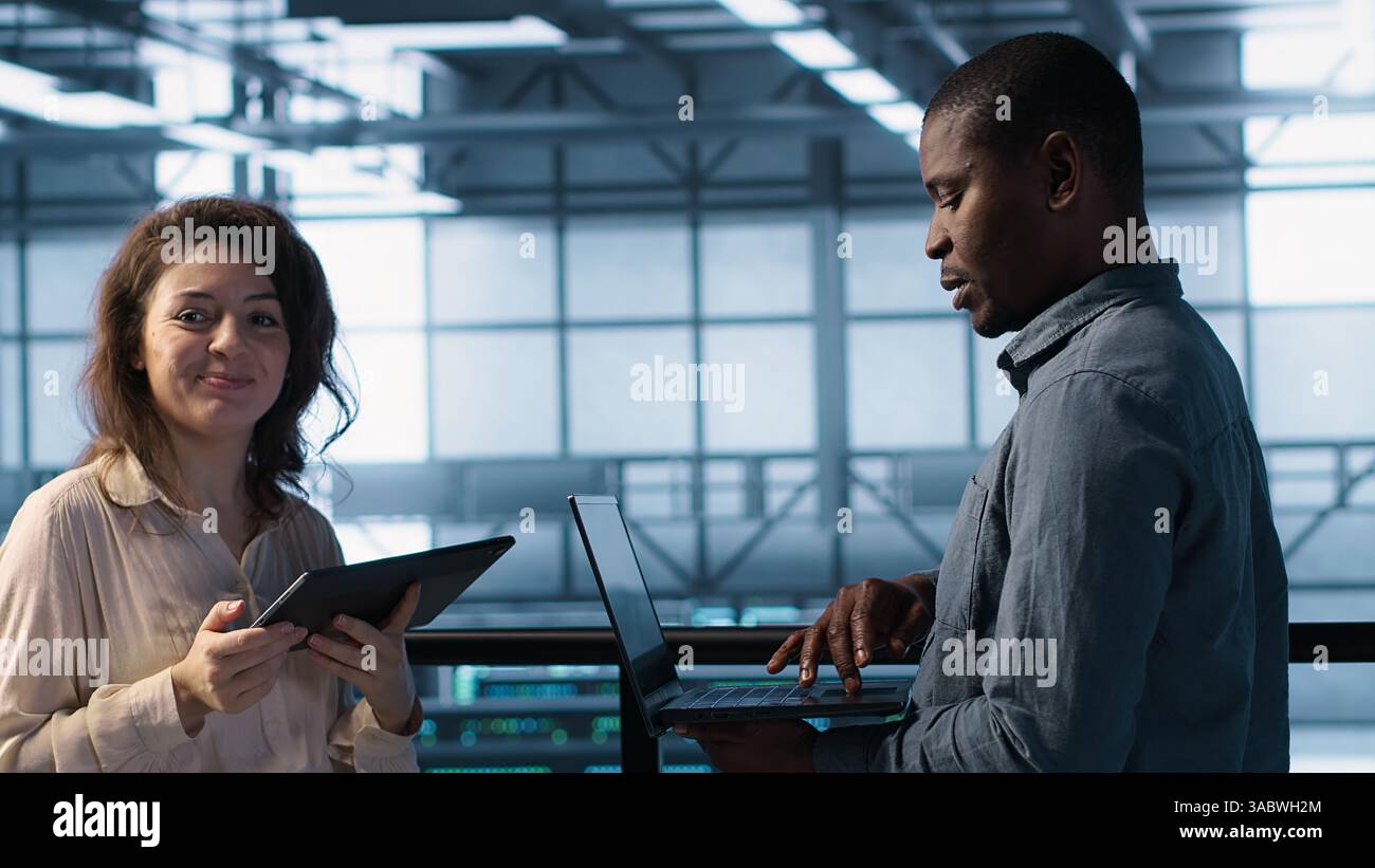 Data scientists in server room using laptop and tablet, executing security patches, verifying ...