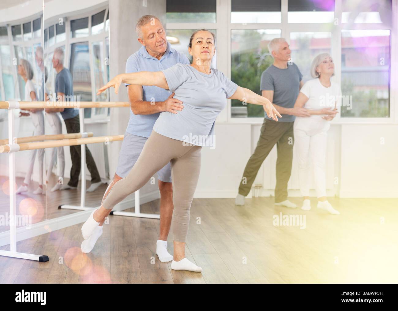 Senior female ballerina with mature male partner practicing arabesque pose during ballet classes ...