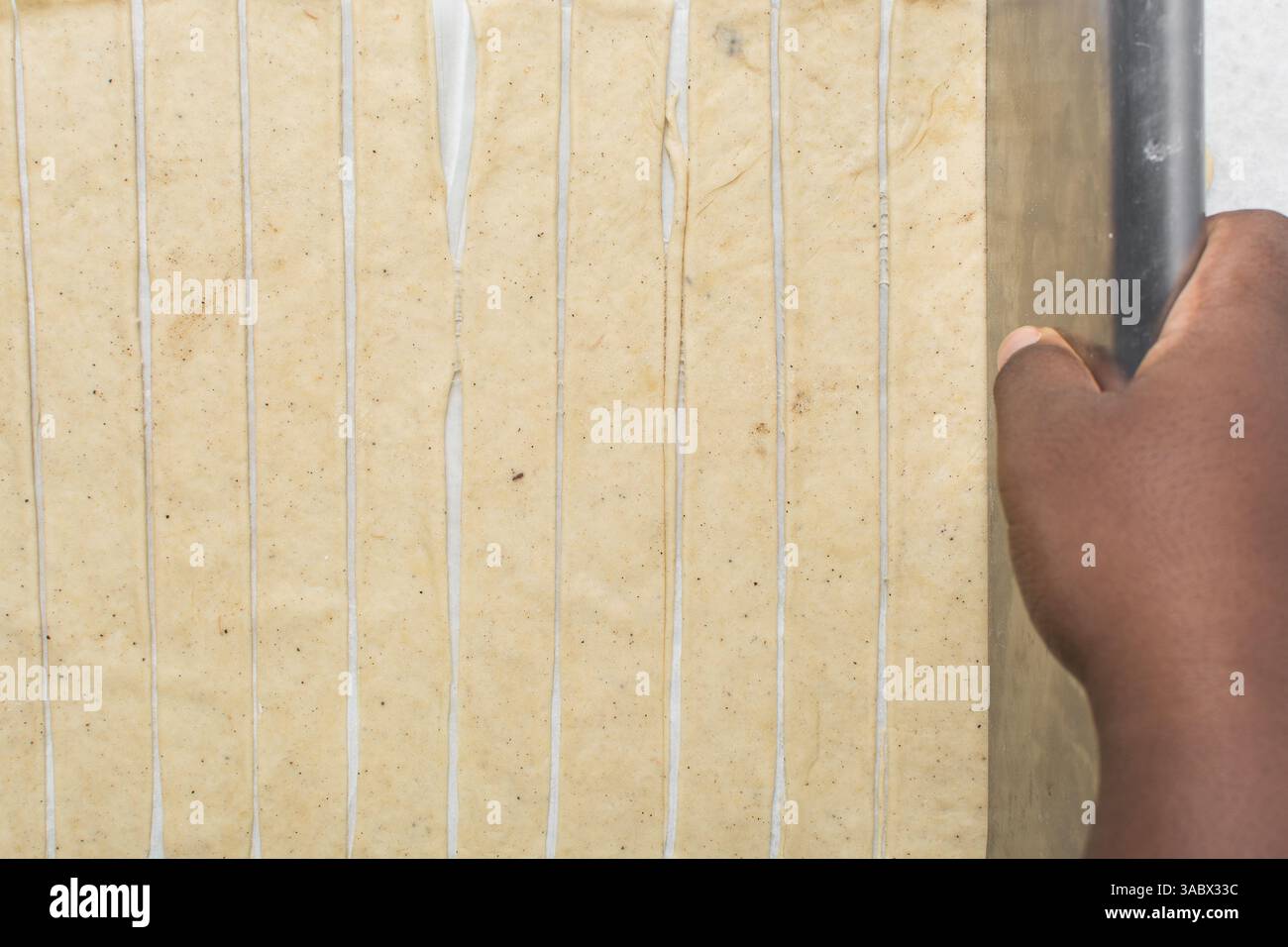 Overhead view of crackers dough on parchment paper being sliced ...