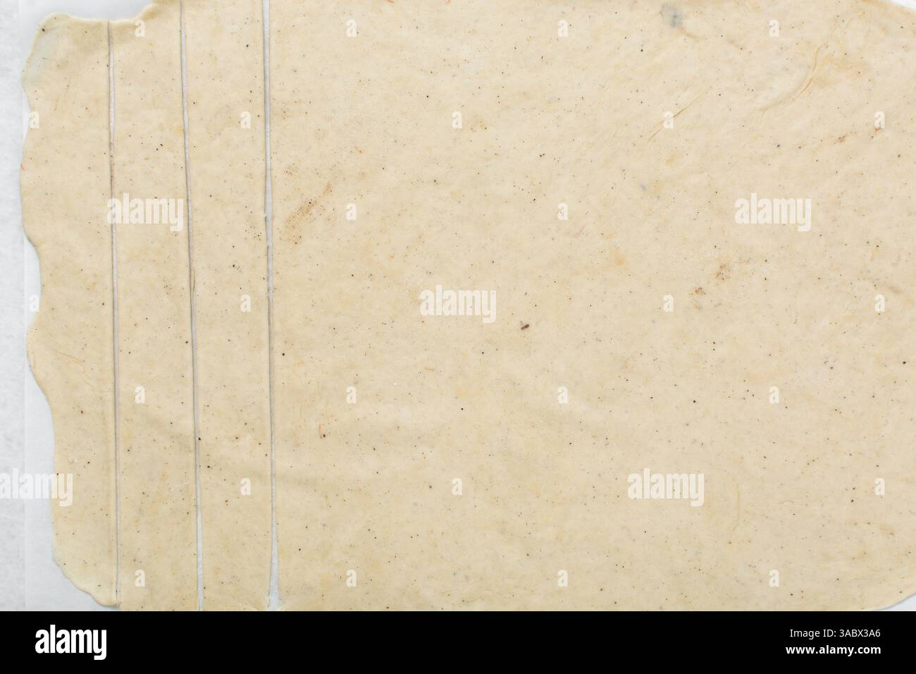 Overhead view of crackers dough on parchment paper being sliced ...