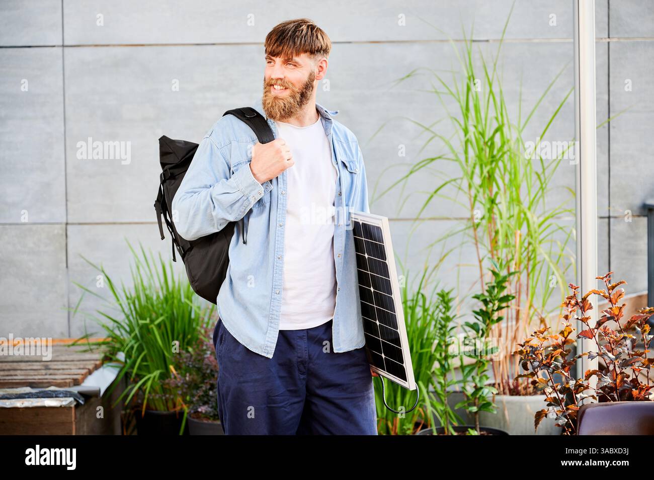 Bearded man carrying solar panel and black backpack, stands in front of ...