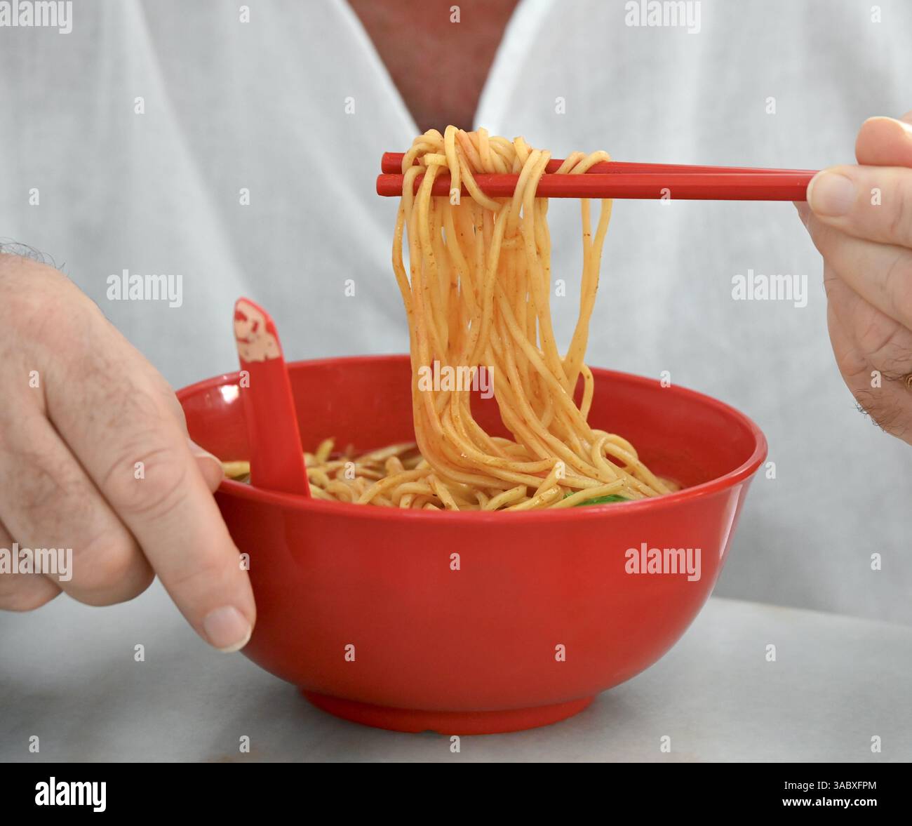 Person is eating noodles using chopsticks from red bowl Stock Photo - Alamy