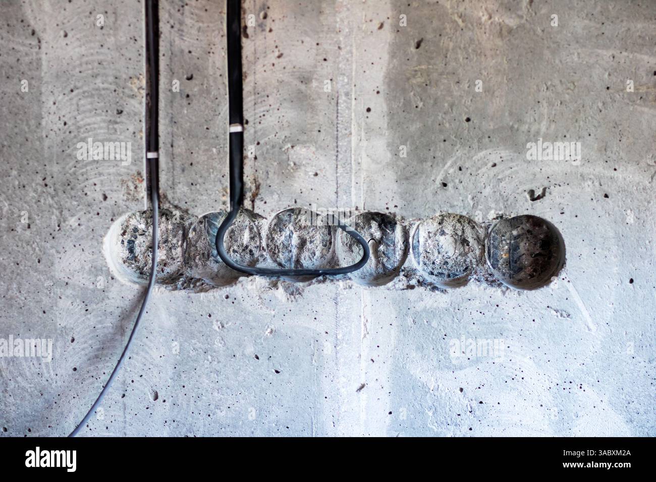 A variety of wires are dangling from a solid concrete wall, creating an ...