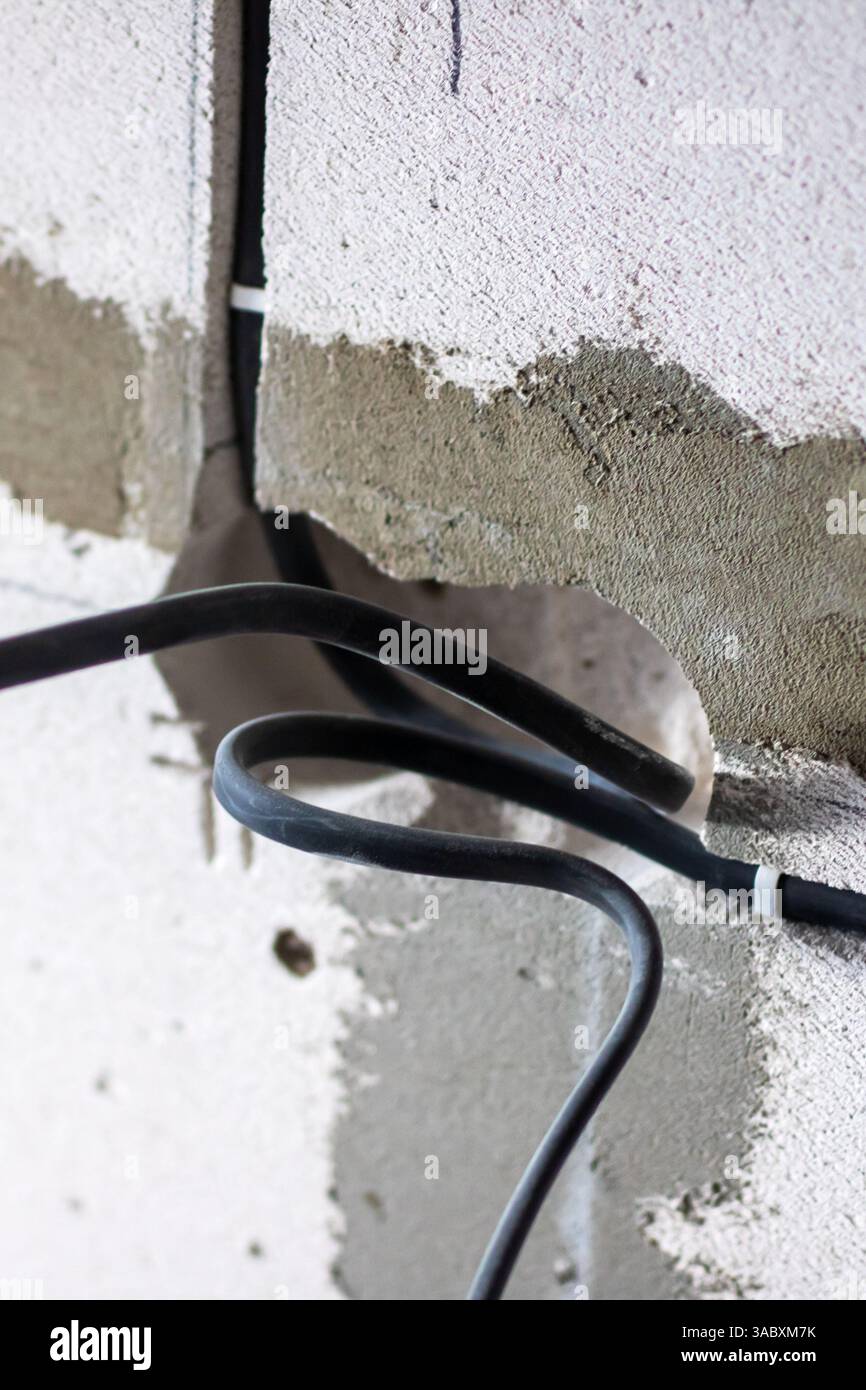 A collection of various wires is hanging down from a concrete wall in ...