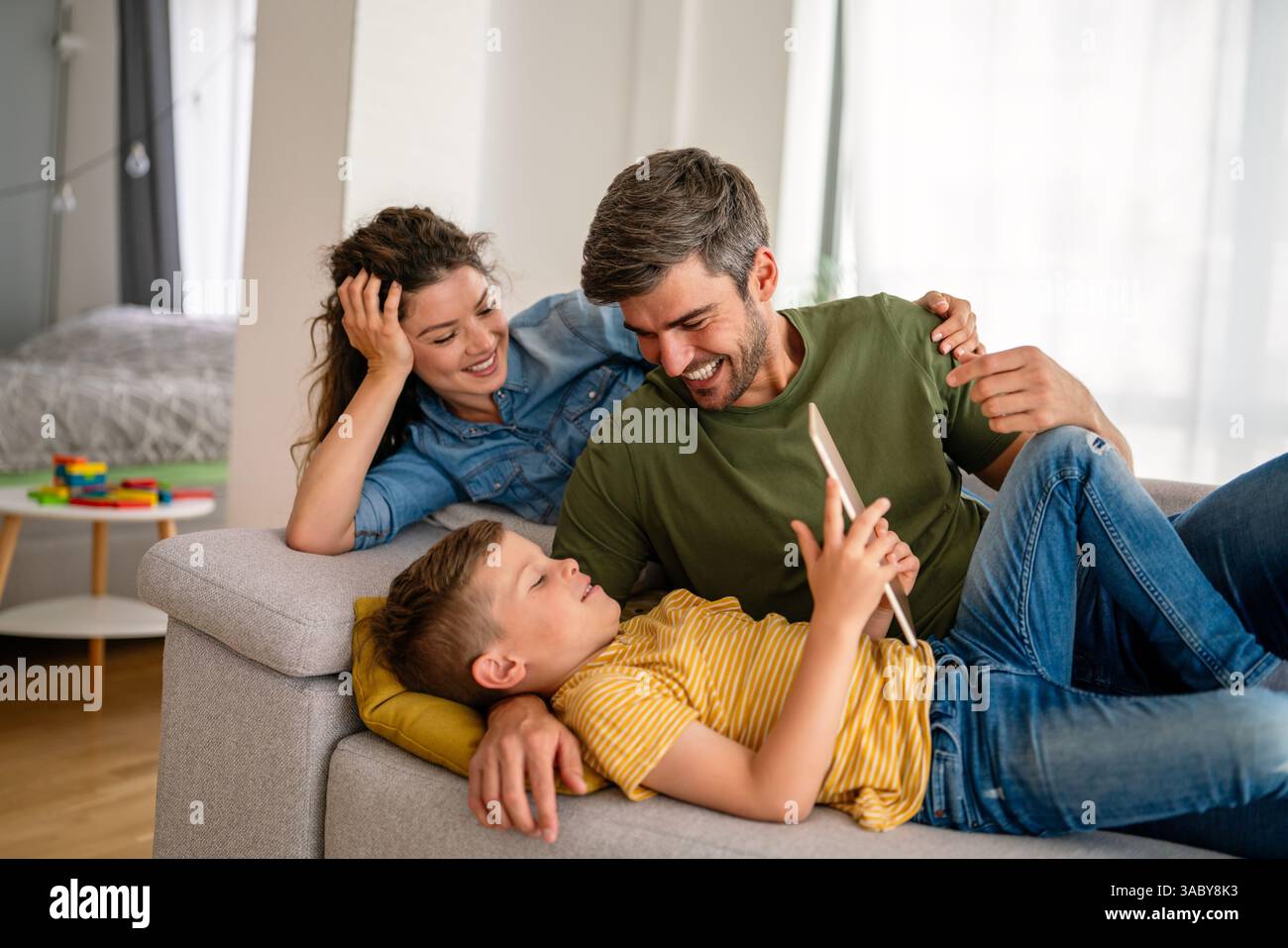 Happy family with kid having fun using tablet together, parents and child laughing relaxing at ...